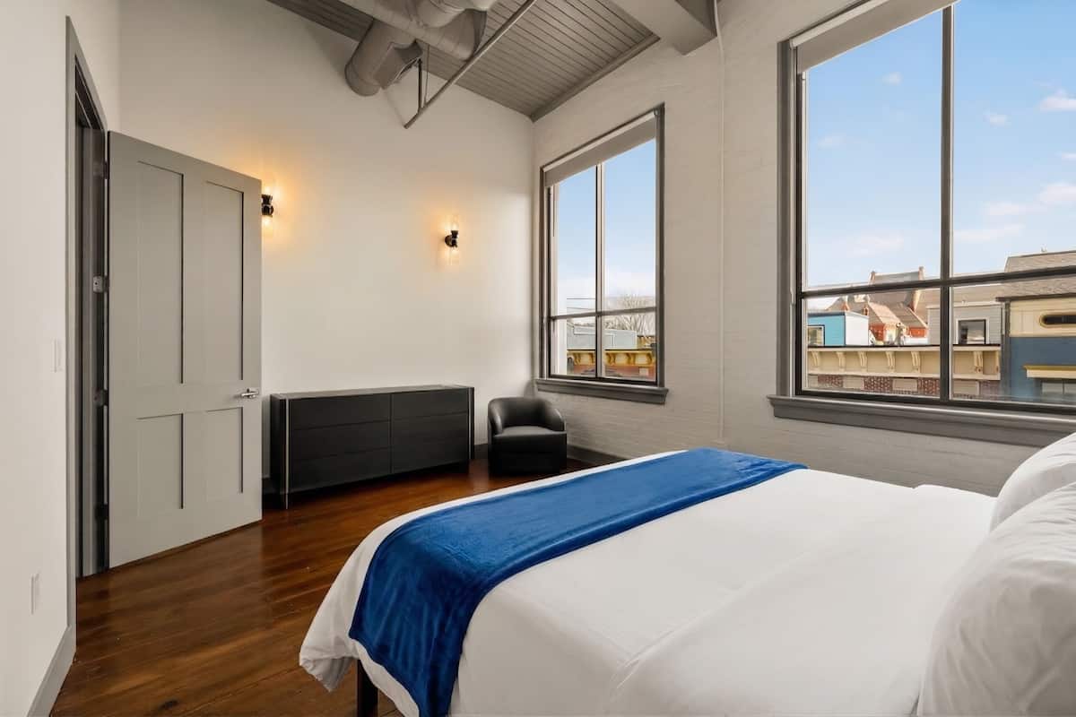 Quarto moderno com uma cama grande, uma cadeira, um radiador e uma janela com vista para edifícios.