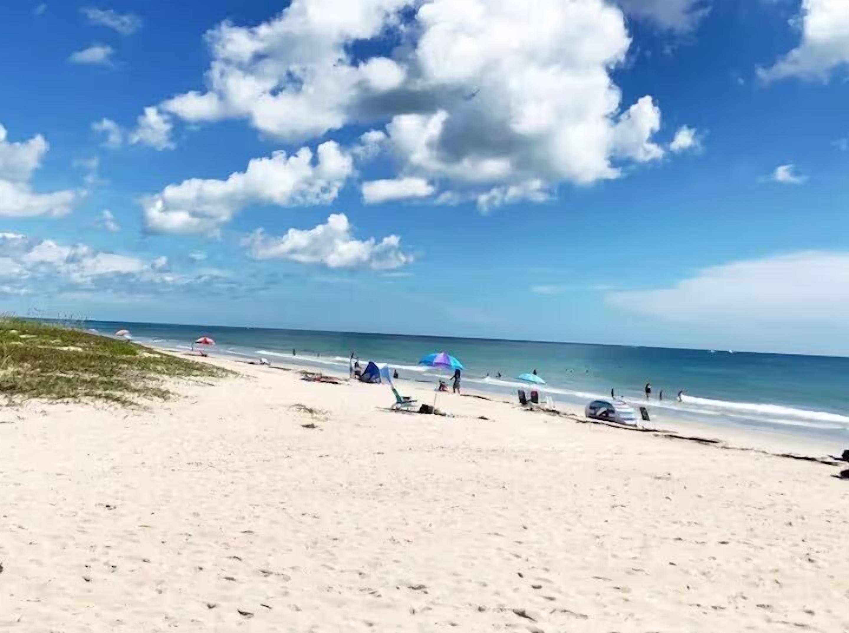 Uma praia com areia, alguns guarda-sóis e céu claro.