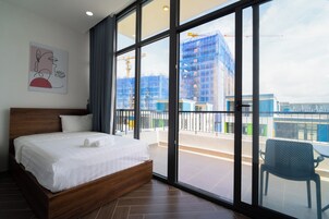 Quarto de hotel com uma cama grande, vista para um canteiro de obras e varanda com uma cadeira.