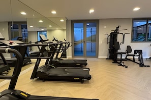 Uma academia com esteiras, aparelhos de musculação e um espelho grande.
