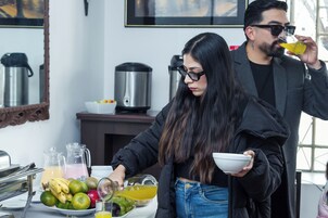 Uma pessoa servindo bebida em uma tigela, uma cafeteira e uma saladeira sobre uma mesa.