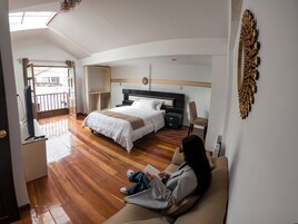 Quarto de hotel com cama, sofá, televisão e varanda.