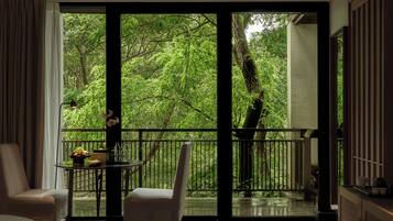 Quarto com vista para uma floresta através de uma porta de correr de vidro. Há uma mesa com um vaso e uma cadeira.
