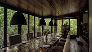 Uma sala de jantar com uma longa mesa de madeira, cadeiras e luminárias pendentes.