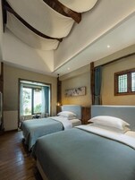 Quarto de hotel com duas camas, janela com cortinas, piso de madeira e teto com vigas aparentes.