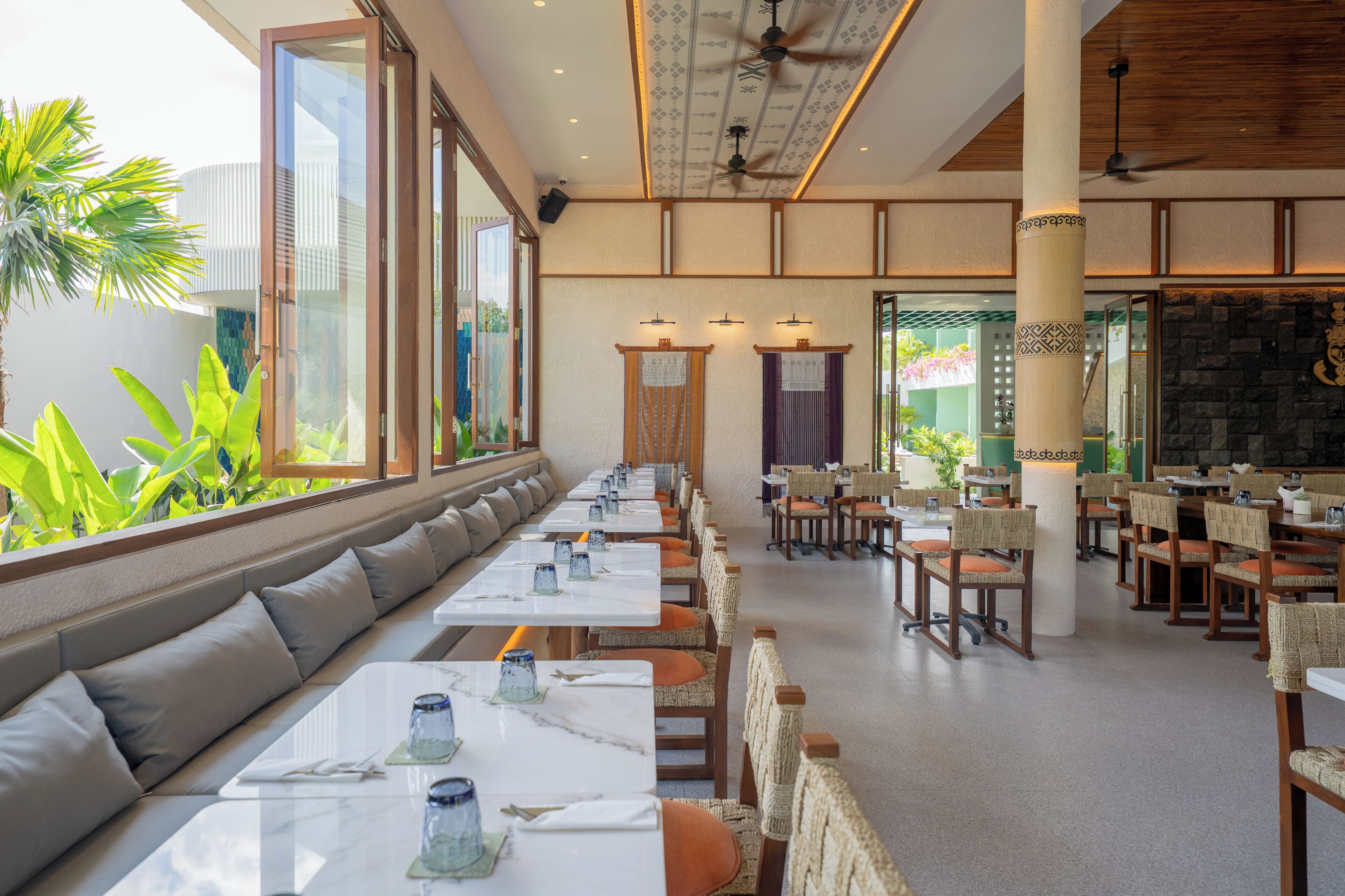 Um restaurante com mesas compridas, assentos acolchoados e amplas janelas.