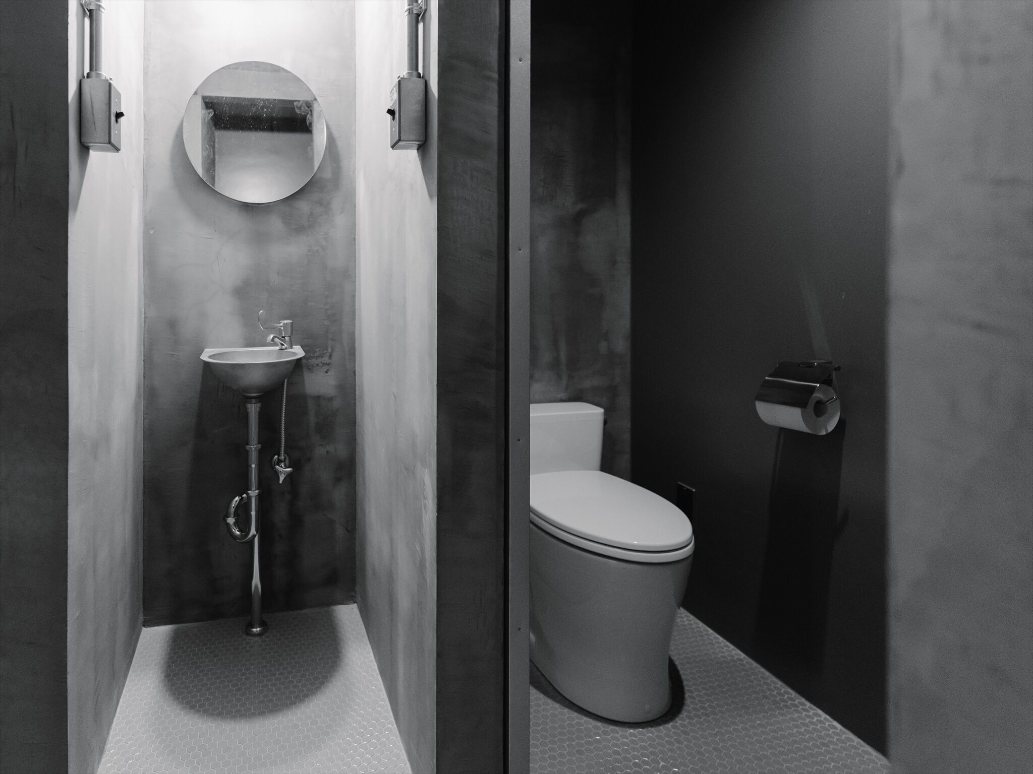 Uma casa de banho moderna com sanita, lavatório, espelho e suporte para papel higiénico.