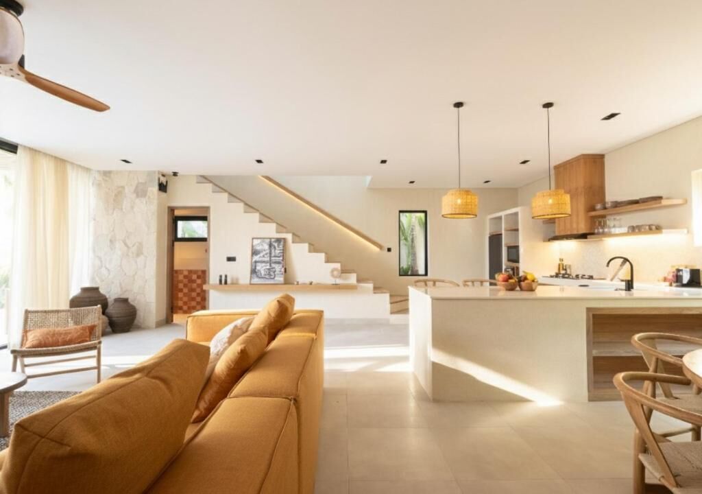 Uma sala de estar moderna com sofá, área de refeições com cadeiras, cozinha com ilha central e escada para um andar superior.
