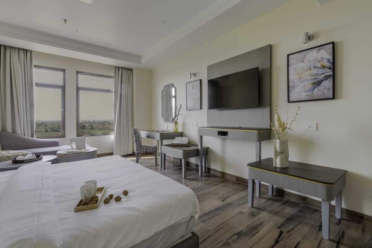 Quarto de hotel com cama grande, escrivaninha, cadeira, televisão e janela com cortinas.