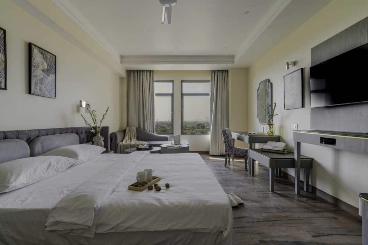 Quarto de hotel com uma cama grande, uma escrivaninha, uma cadeira, uma televisão e vista para o exterior.