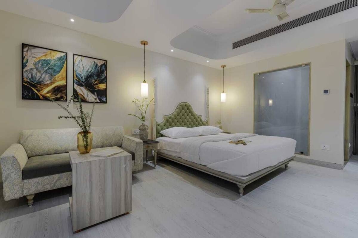 Quarto com cama, sofá, mesa lateral e duas pinturas fixadas na parede.