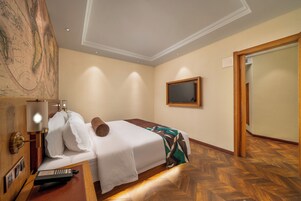 Quarto de hotel com cama, cabeceira de madeira, mapa na parede, televisão e piso de madeira.