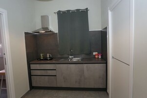 Uma cozinha compacta com pia, armários, fogão e janela com cortina.
