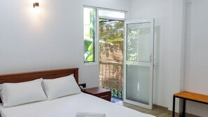 Quarto com cama de madeira, mesa de cabeceira, um banco e porta de vidro deslizante que dá para uma varanda.