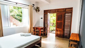 Quarto com cama, mesa e cadeira. Há uma janela e uma porta que dá para uma área externa.