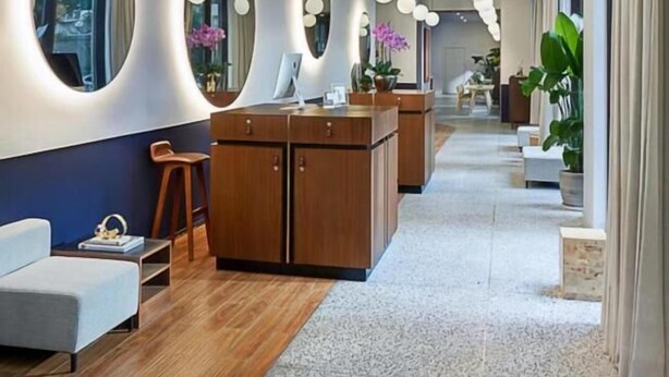 Um hall de hotel moderno com espelhos redondos, balcão de recepção em madeira e um corredor longo com assentos.