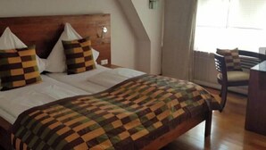 Quarto com cama, cabeceira de madeira, colcha xadrez, uma cadeira e janela com cortinas.