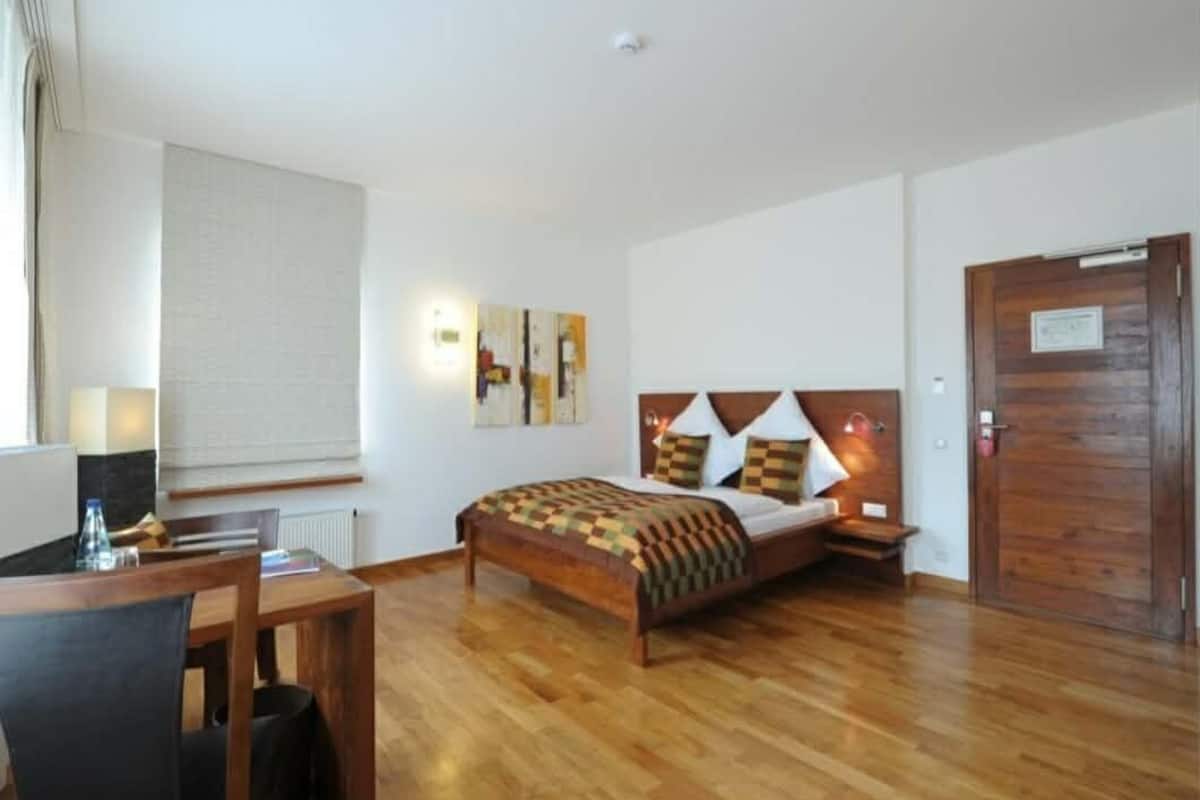 Quarto com cama de madeira, escrivaninha e cadeira, janela com persianas e porta.