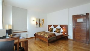 Quarto com cama de madeira, escrivaninha e cadeira, janela com persianas e porta.