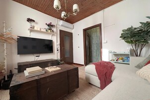 Uma sala de estar moderna com televisão de tela plana, móveis de madeira, um sofá branco e uma planta grande.