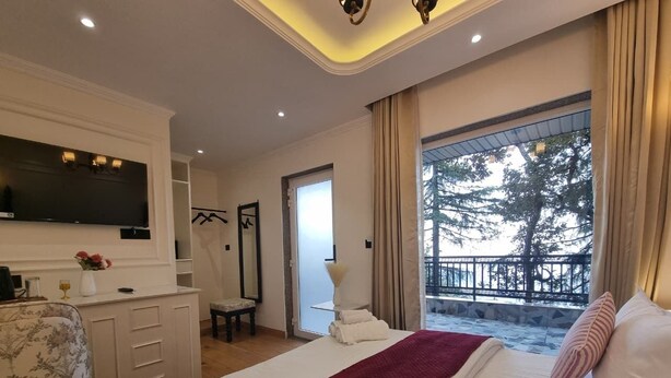 Quarto de hotel com cama, escrivaninha, espelho, TV e varanda com vista.