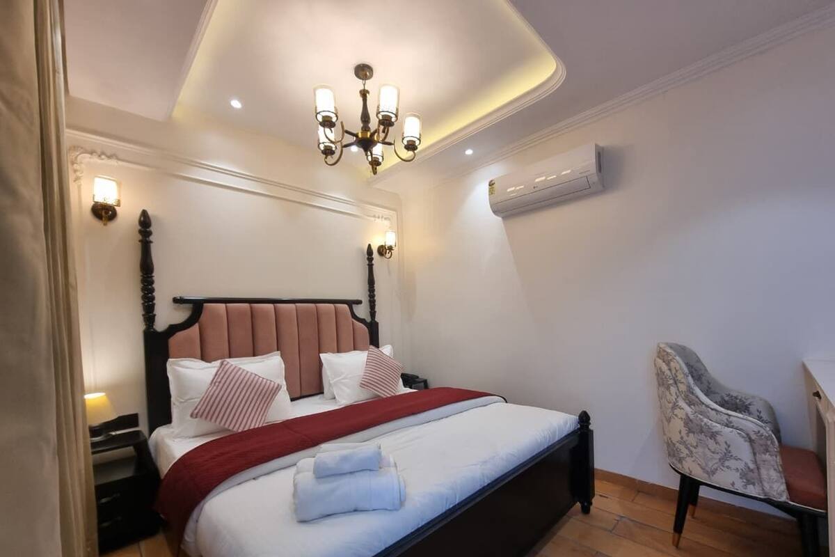 Uma cama bem arrumada com cabeceira, luminária de cabeceira e uma cadeira.