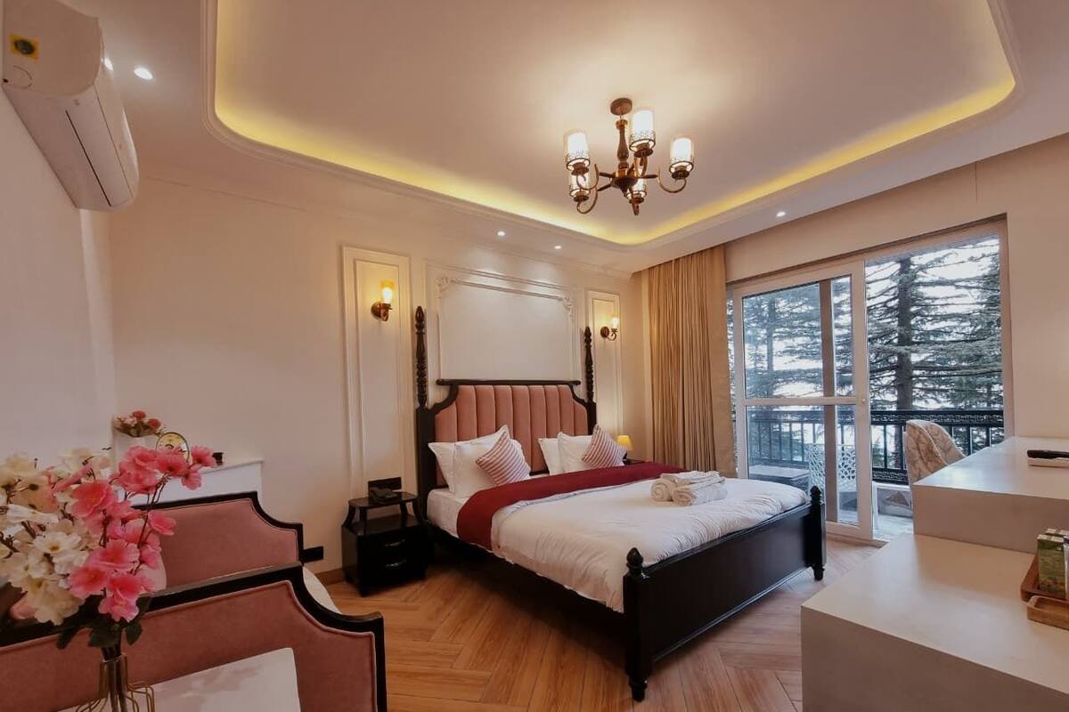 Quarto moderno com uma cama grande, mesas de cabeceira, escrivaninha e vista para árvores pela janela.