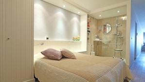 Quarto com cama, mesa de cabeceira, espelho e área de chuveiro.