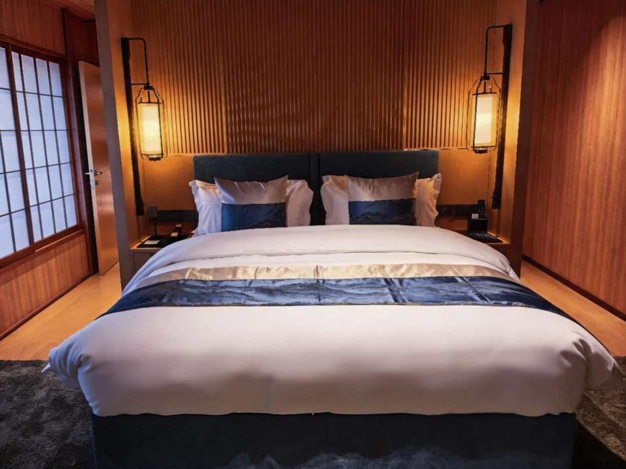 Uma cama com cabeceira, duas mesas de cabeceira e luminárias fixadas na parede.