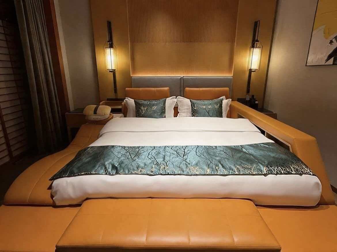 Uma cama grande com cabeceira, duas mesas de cabeceira e duas luminárias fixadas na parede.
