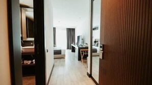 Quarto de hotel com piso de madeira, uma cama, uma escrivaninha e uma televisão.