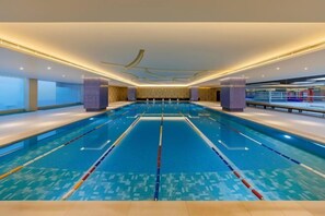 Piscina interna com pistas demarcadas, piso revestido e design moderno no teto.