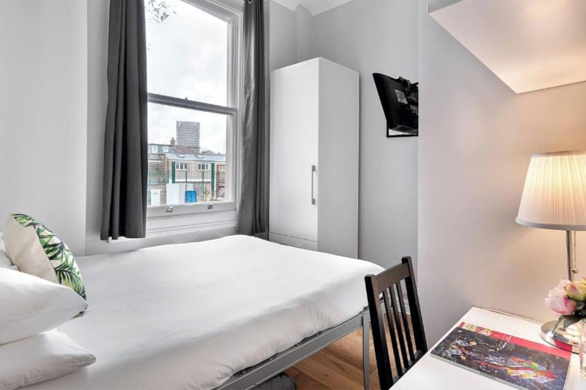 Quarto com cama, escrivaninha, cadeira, guarda-roupa e janela com cortinas.