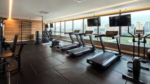 Academia moderna com esteiras, máquinas de peso e vista para a cidade.