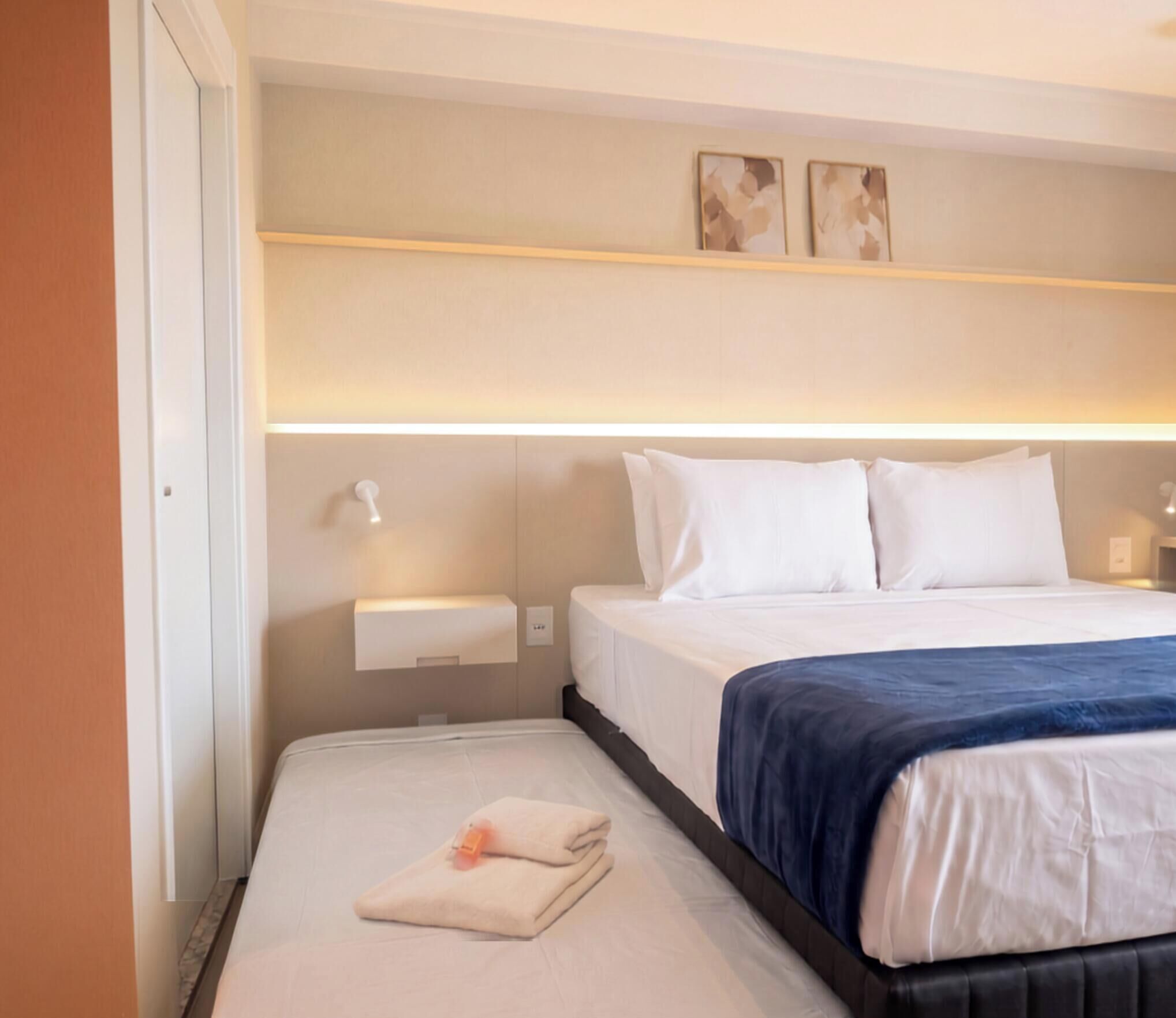 Quarto de hotel com uma cama, mesas de cabeceira e uma prateleira na parede.