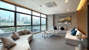 Uma sala de estar moderna com um sofá curvo, uma mesa de centro e um sofá com almofadas. Grandes janelas proporcionam vista para a cidade.