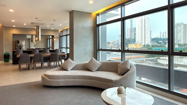 Uma sala de estar moderna com um sofá curvo, um espaço de jantar com mesa e cadeiras, e grandes janelas com vista para a cidade.