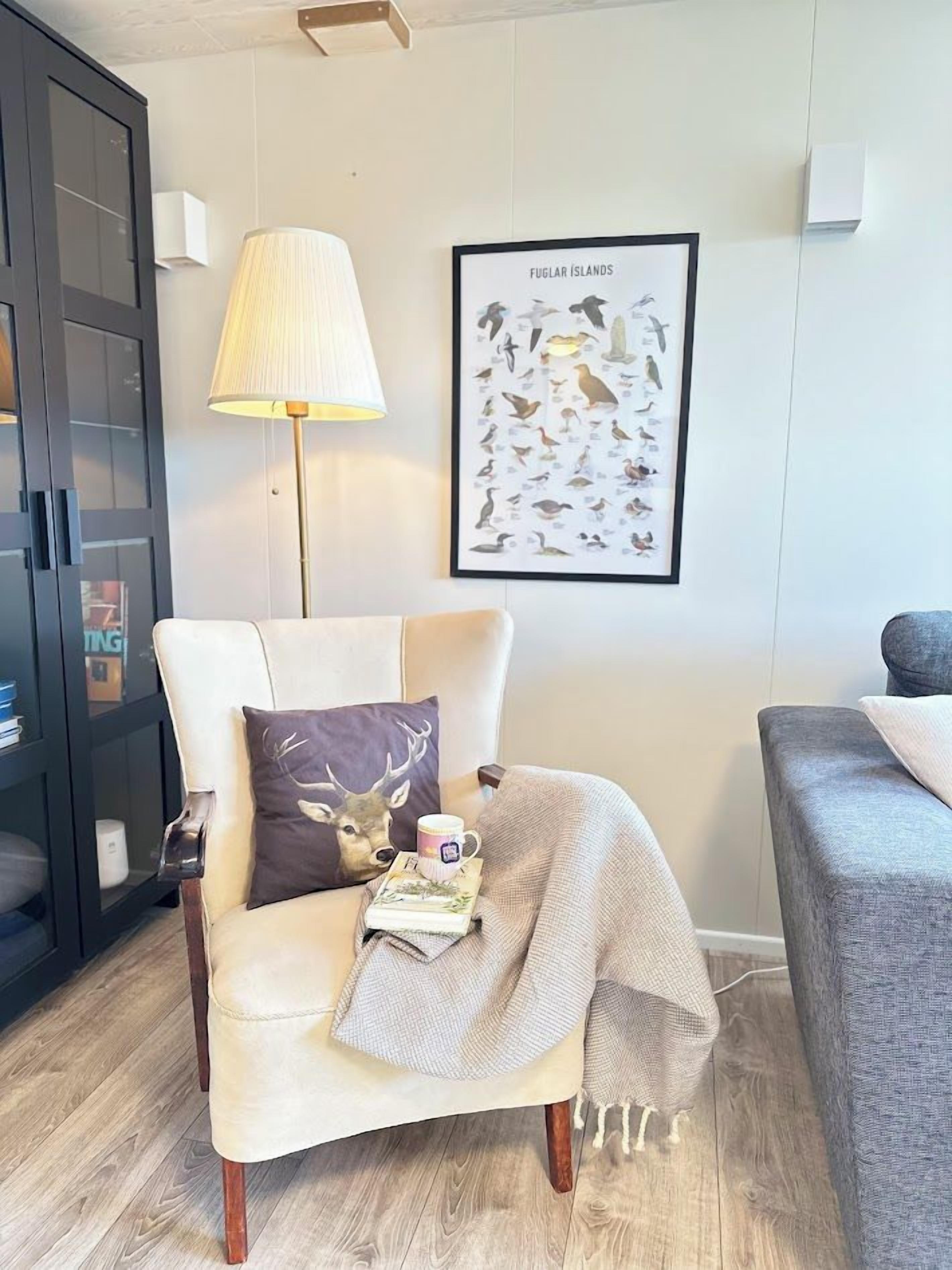 Quarto com poltrona bege, pôster de animais emoldurado, luminária e estante de livros.