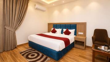 Quarto de hotel com uma cama, mesa de cabeceira, cadeira, mesa de centro e aparelho de ar condicionado.