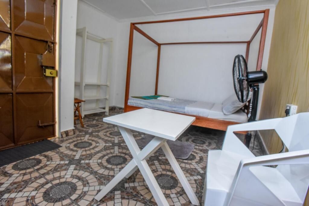 Quarto com cama de dossel, uma mesinha, um ventilador e piso estampado.