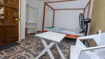 Quarto com cama de dossel, uma mesinha, um ventilador e piso estampado.