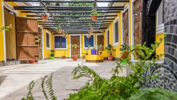 Um pátio coberto com plantas em vasos, chão de pedra e paredes amarelas.