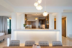 Cozinha moderna com ilha central, iluminação pendente e área de refeições com mesa e cadeiras.