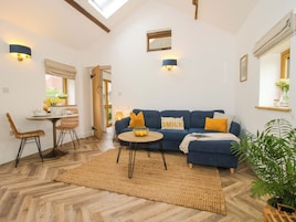 Uma sala de estar aconchegante com um sofá azul, uma mesa de jantar com cadeiras, uma mesa de centro e uma janela grande com cortinas.
