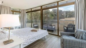 Um quarto com cama, mesa de cabeceira, luminária, sofá e varanda com cadeiras.