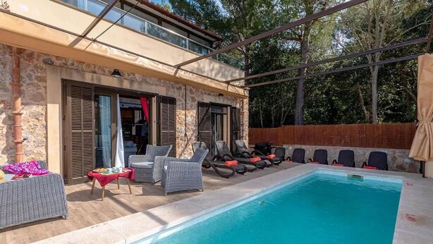 Uma área junto à piscina, com piscina, mobiliário de exterior e um edifício de pedra com portadas.