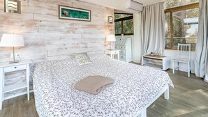 Quarto com cama grande, mesas de cabeceira, um criado-mudo, janela com cortinas e vista para o exterior.