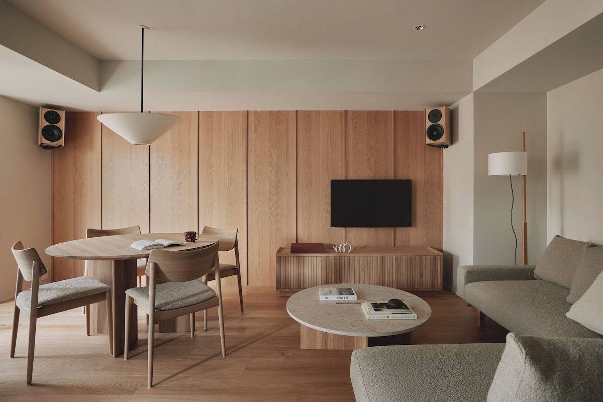 Uma sala de estar moderna com painel de madeira, TV de tela plana, mesa de centro redonda e um sofá.