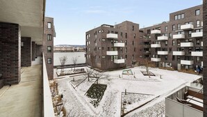 Um edifício residencial com vários andares, varandas, um pátio com neve e um rio ao fundo.
