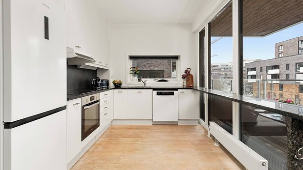 Uma cozinha moderna com armários brancos, bancada preta e janela com vista para a cidade.